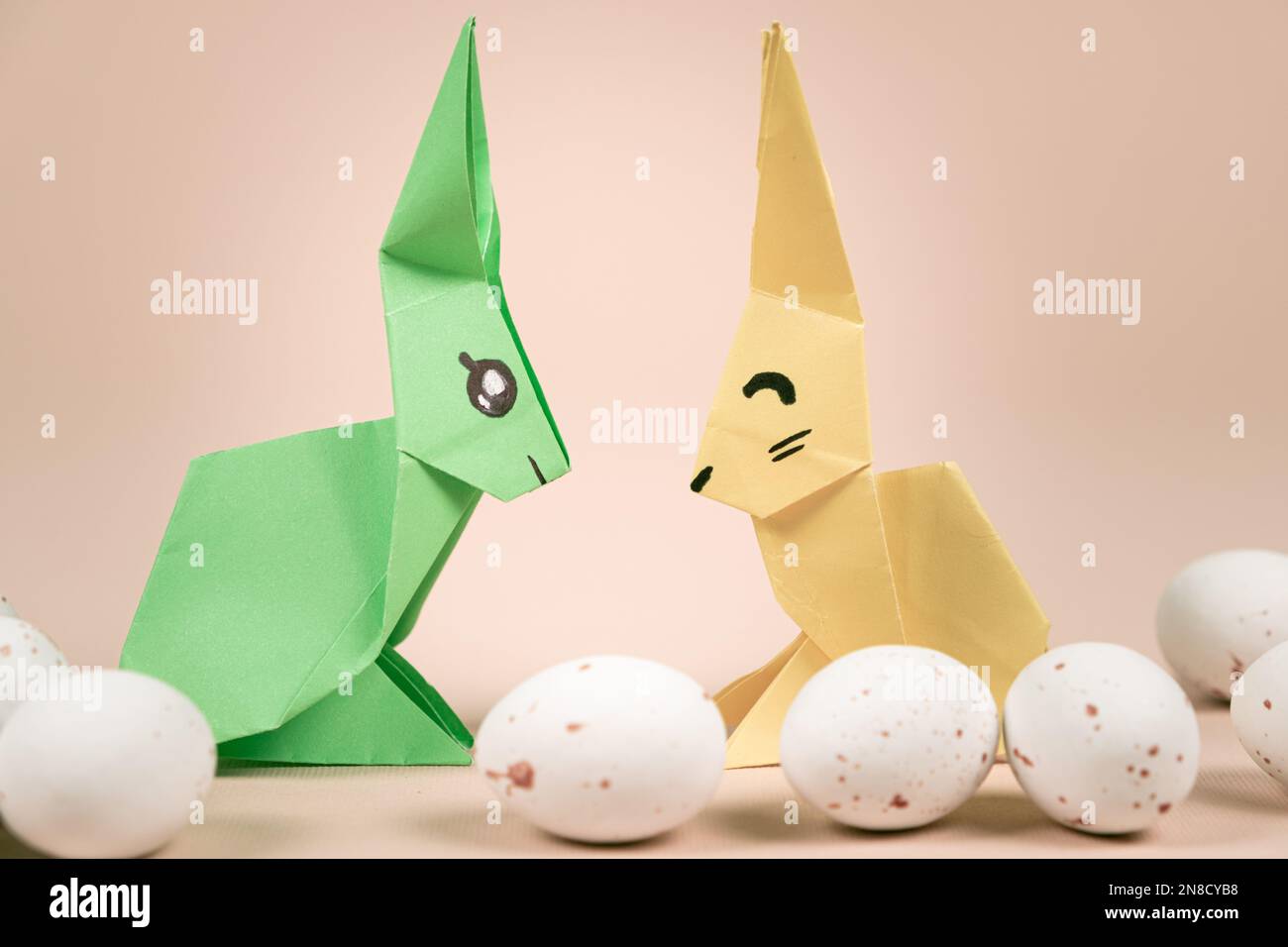Two paper origami bunnies and an Easter egg on a beige background ...
