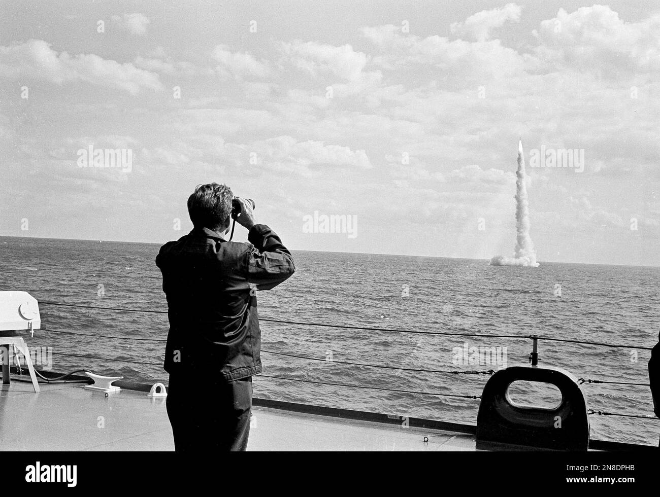 President John F. Kennedy, wearing a windbreaker, watches through ...