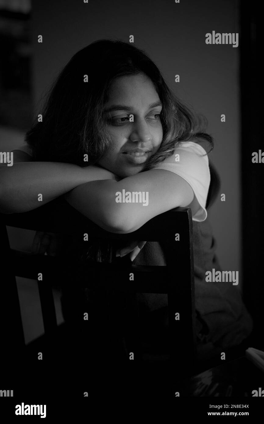 A vertical grayscale of a smiling female sitting on a chair with arms ...