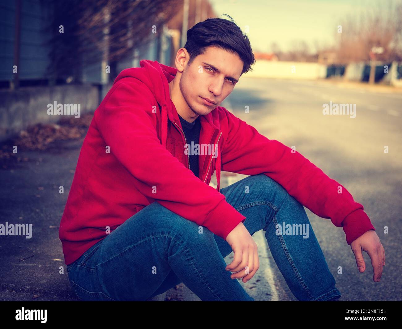 Attractive young man sitting on street curb Stock Photo - Alamy
