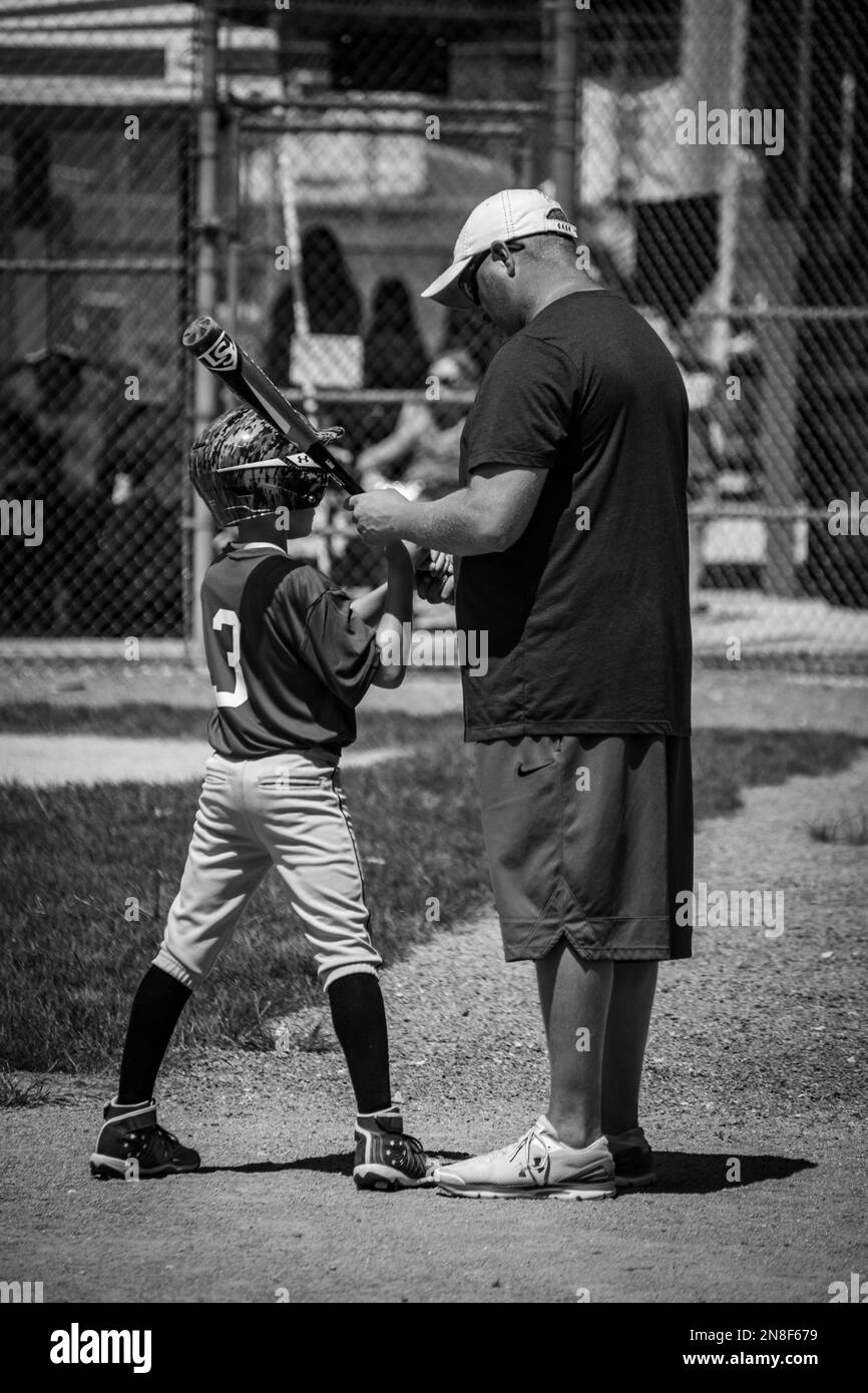 A monochrome shot of a father showing his son how to hold a baseball ...