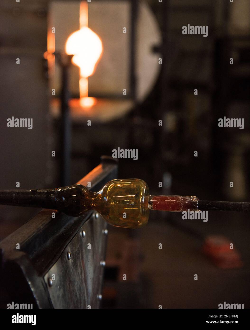 A professional glass blower holding glass mold with high heat fire for ...
