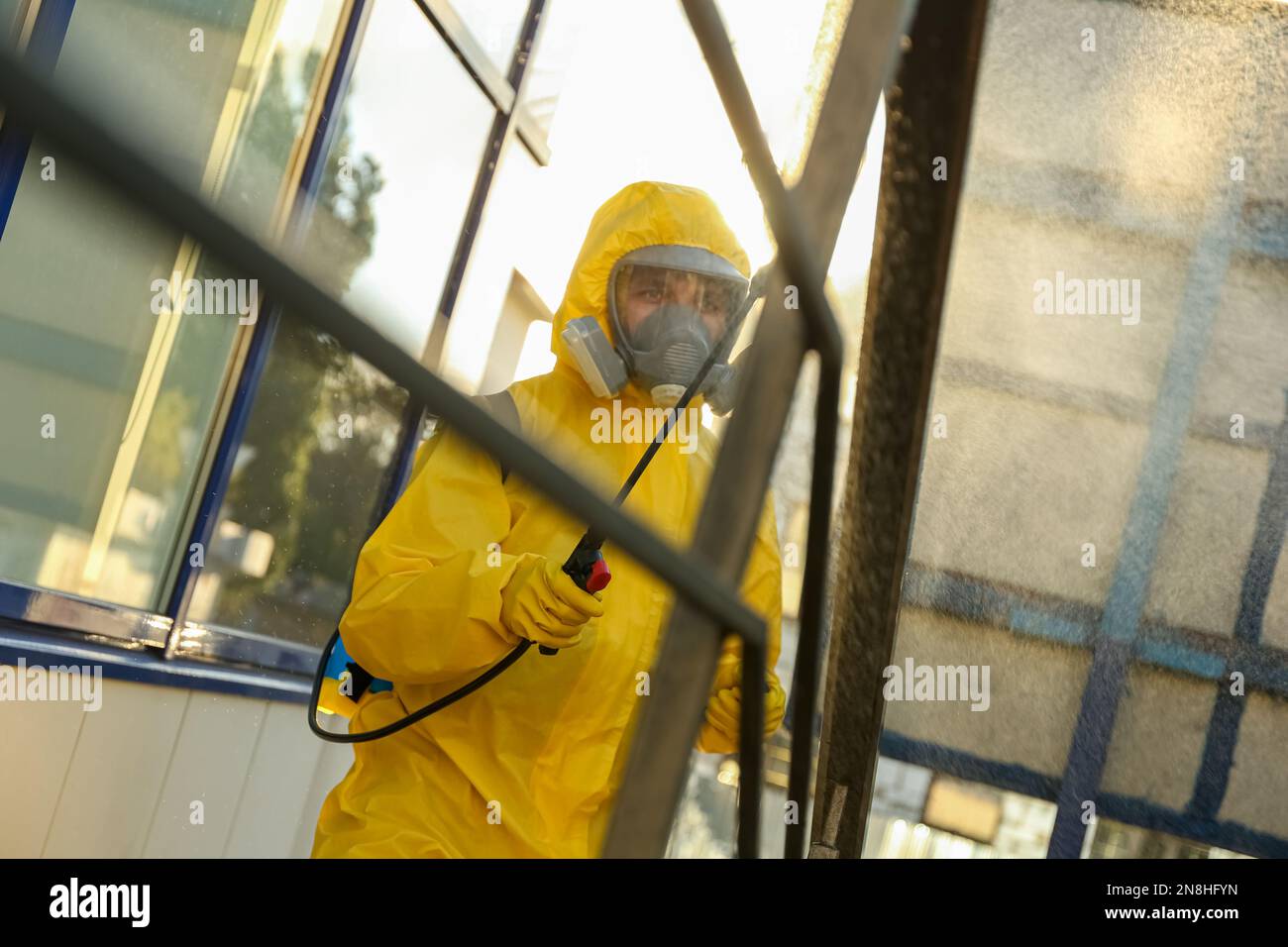 Person in hazmat suit with disinfectant sprayer cleaning metal railing ...