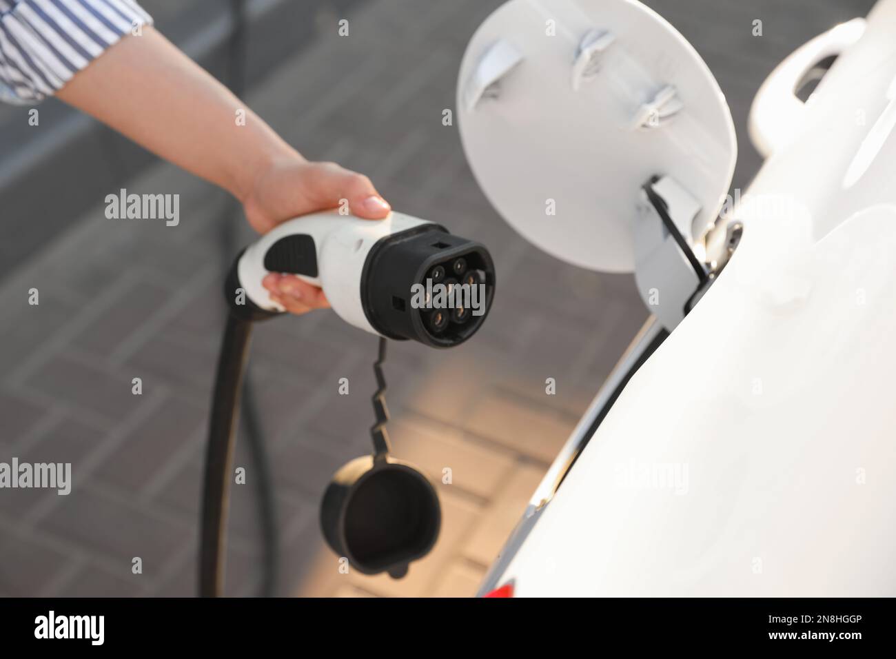 Woman inserting plug into electric car socket at charging station ...