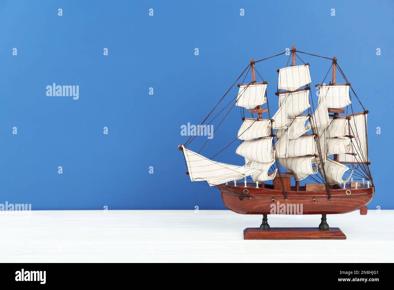 Miniature model of old ship with white sails on table against blue ...