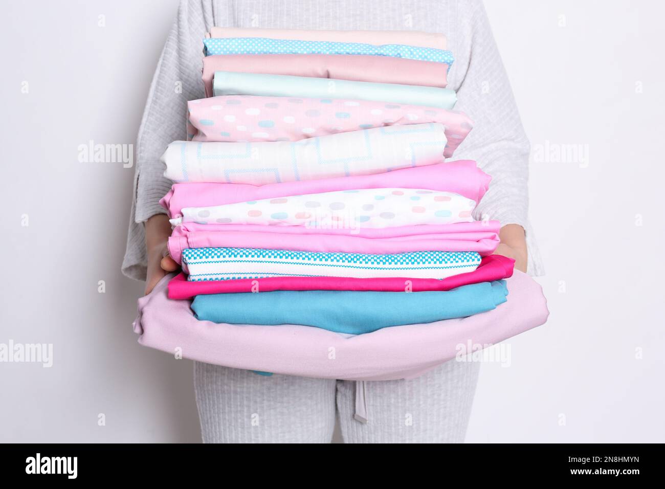 Woman holding stack of clean bed linens on white background, closeup ...