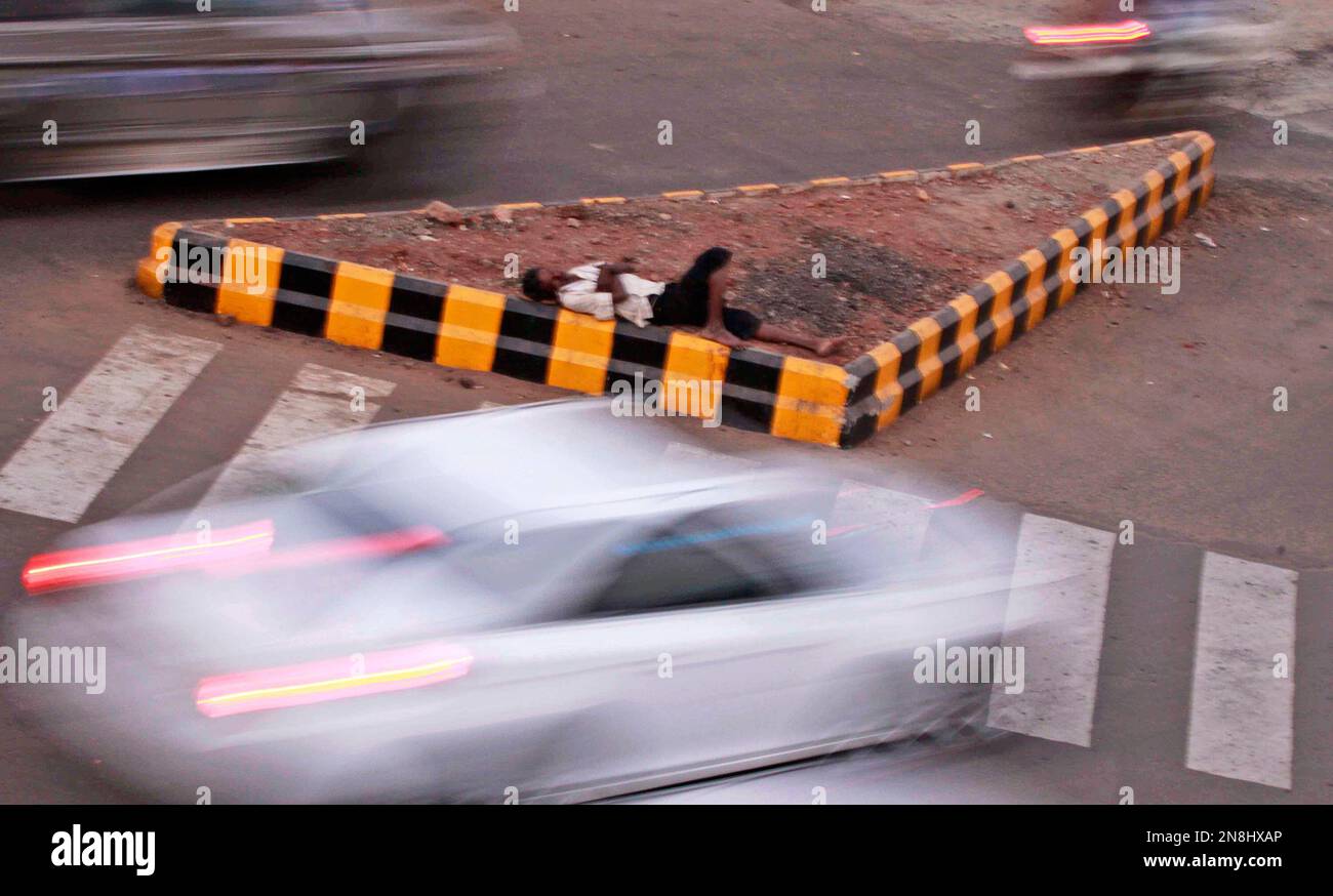 An Indian man sleeps on a road divider of a busy street in Bhubaneswar ...
