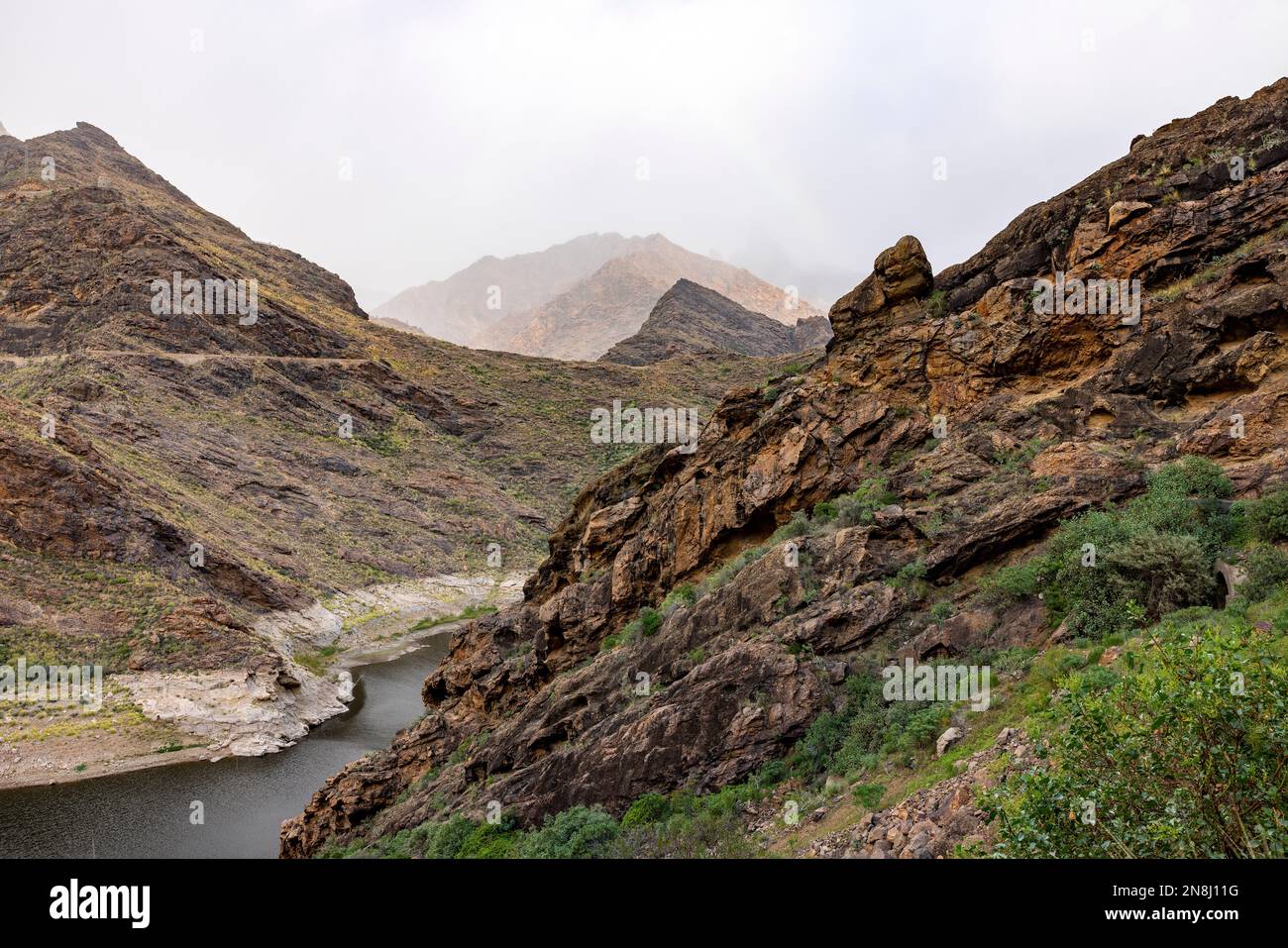Mountains with some grass, brown rocks on rainy day. Rainbow on the ...