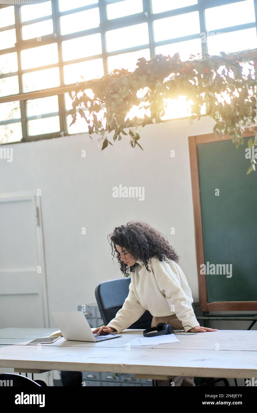 Young woman school teacher or worker standing at desk using laptop in ...
