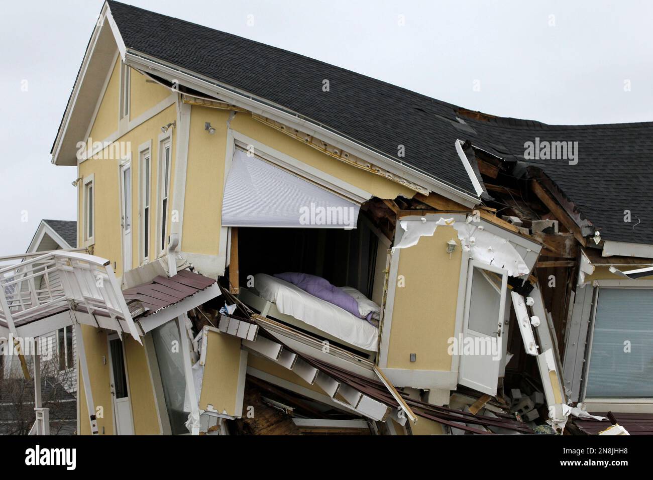A bed sits precariously exposed in a partially collapsed home in the ...
