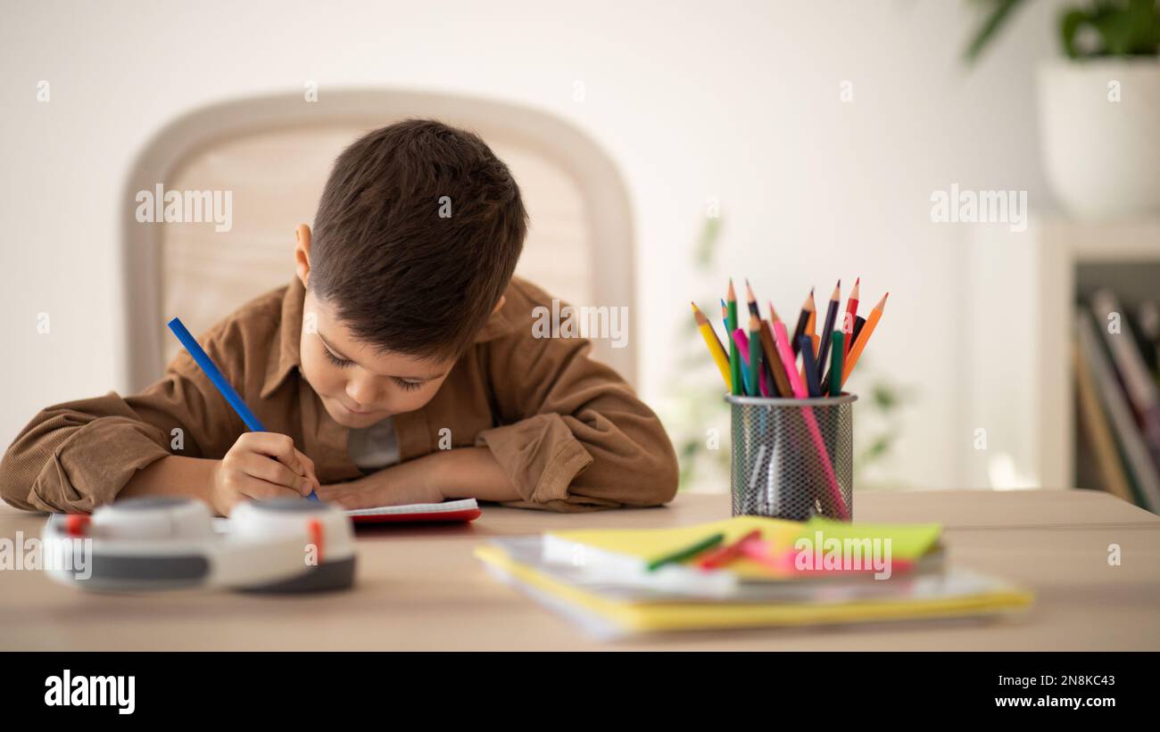 Busy serious european small kid drawing, writing, studying at table in ...