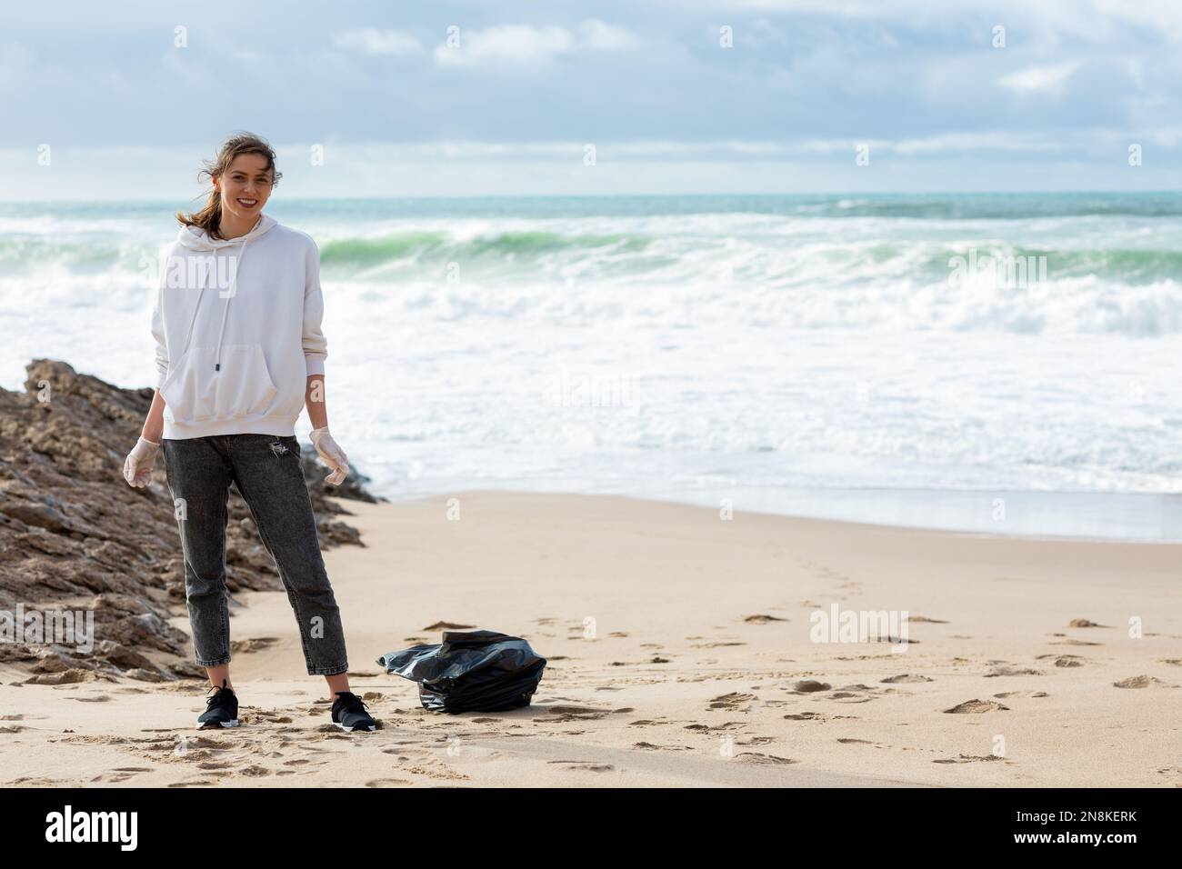 Young female activist standing with plastic bag on the beach by seaside ...