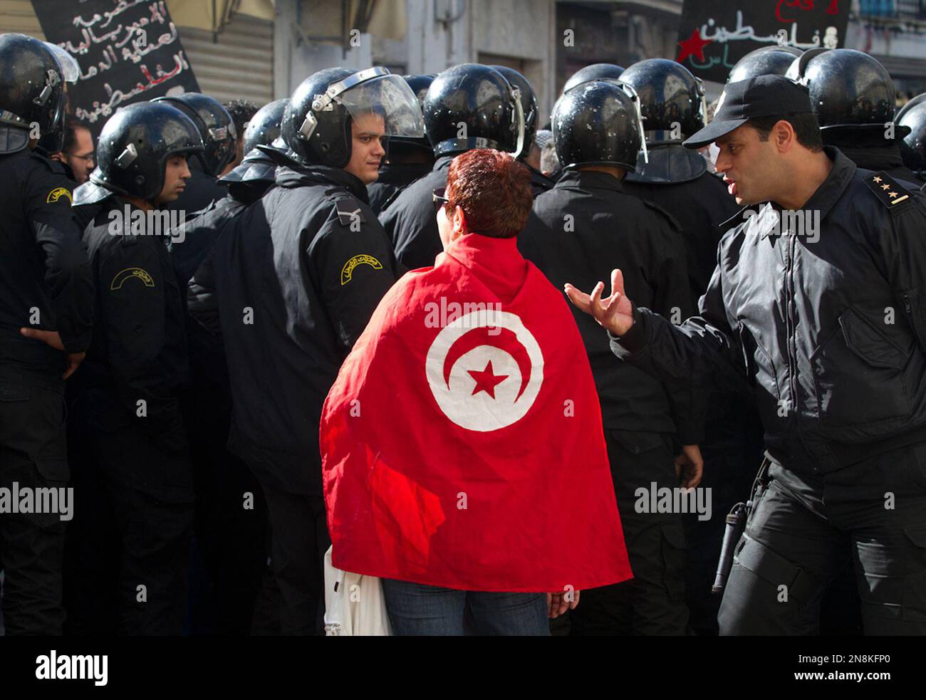 A Tunisian protester drapped in a national flag, argues with riot ...