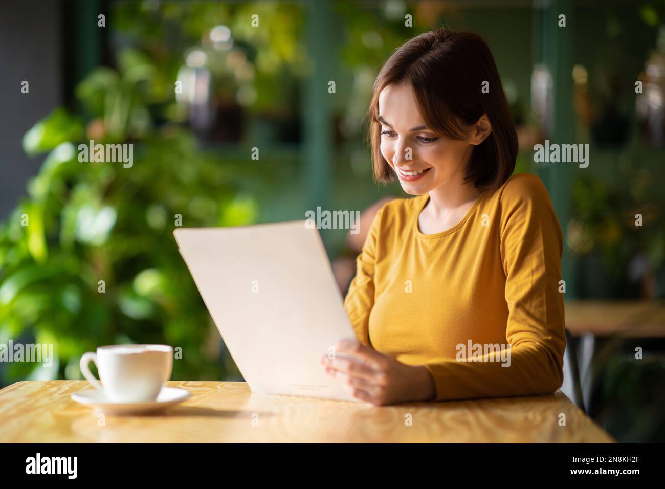 Pretty young woman chilling at cafe, drinking coffee, reading menu ...