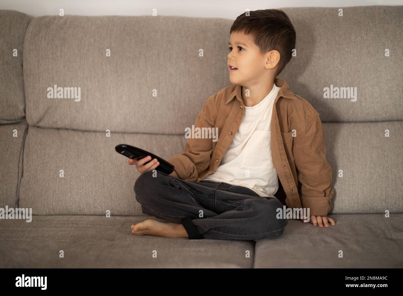 Serious cute european small kid uses remote control, switches channel ...