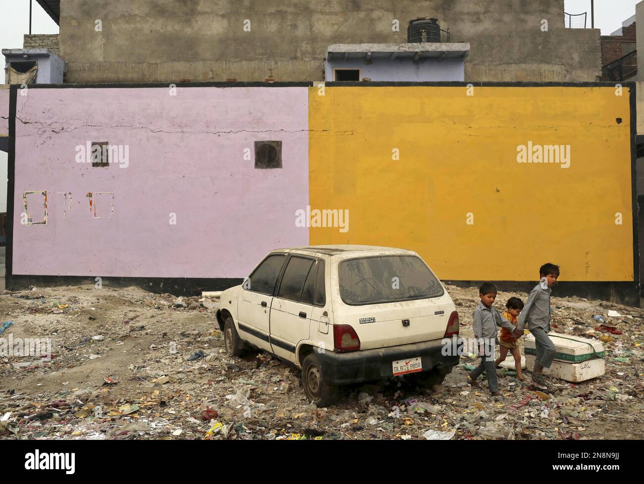 Indian boys walk past an abandoned and damaged car in a poor ...