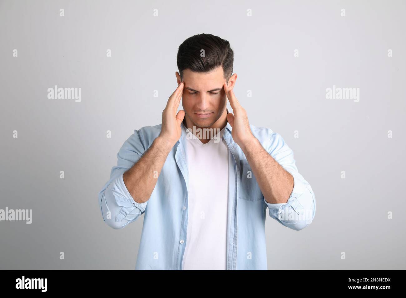 Man rubbing his temples on light background. Stress relief Stock Photo ...
