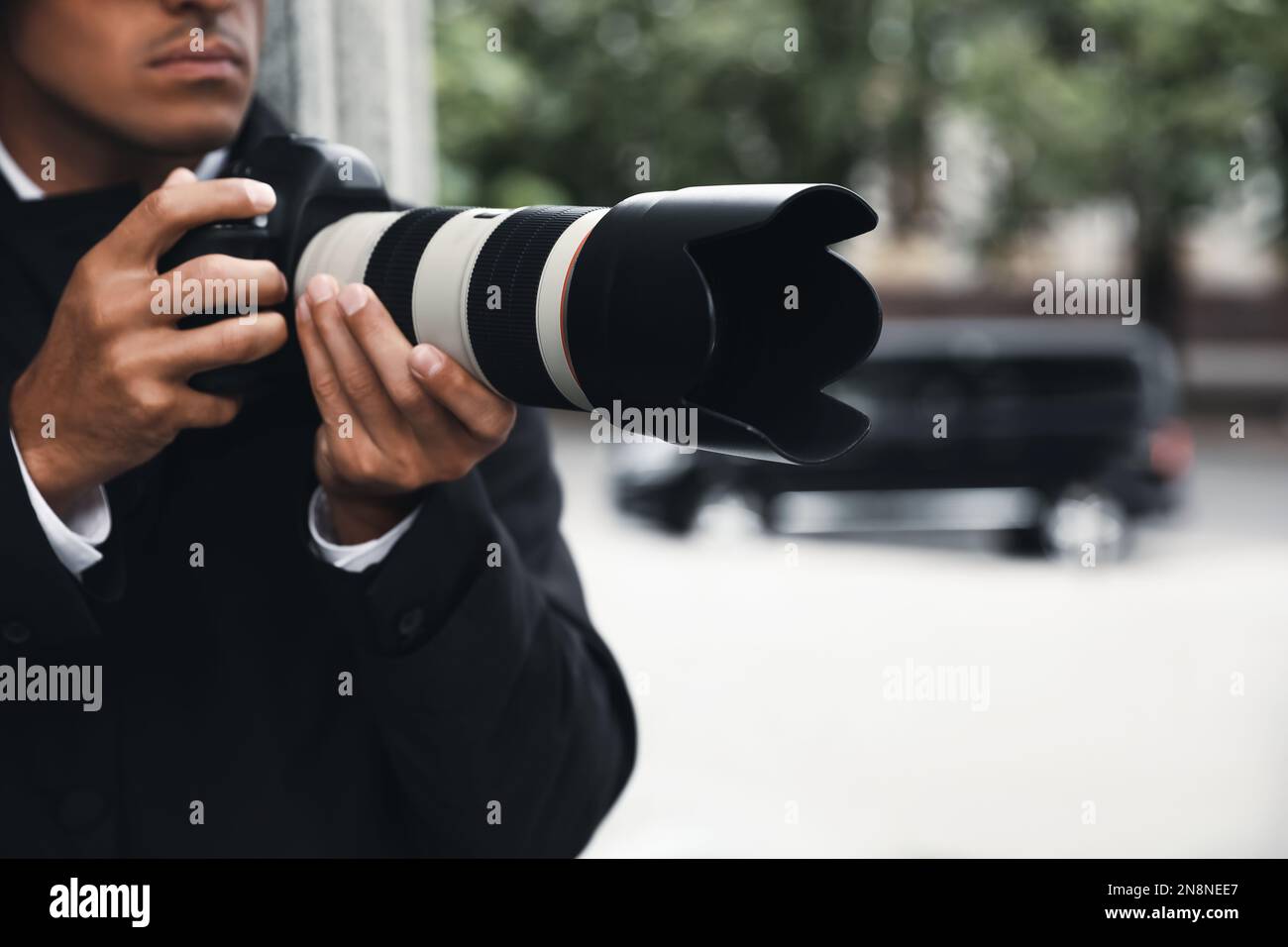 Private detective with modern camera spying outdoors, focus on lens ...