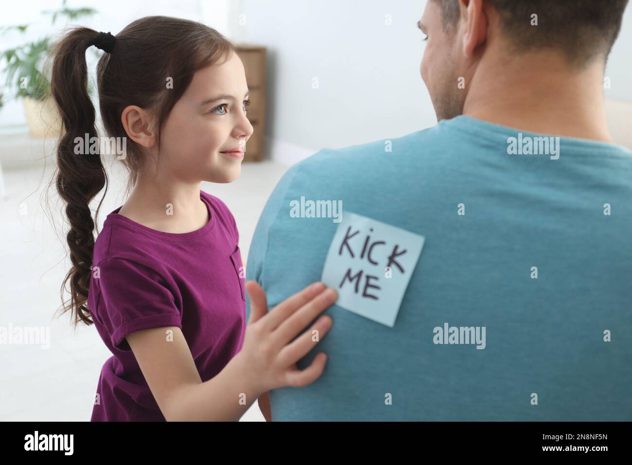 Cute little girl sticking note with words Kick Me to father's back at ...