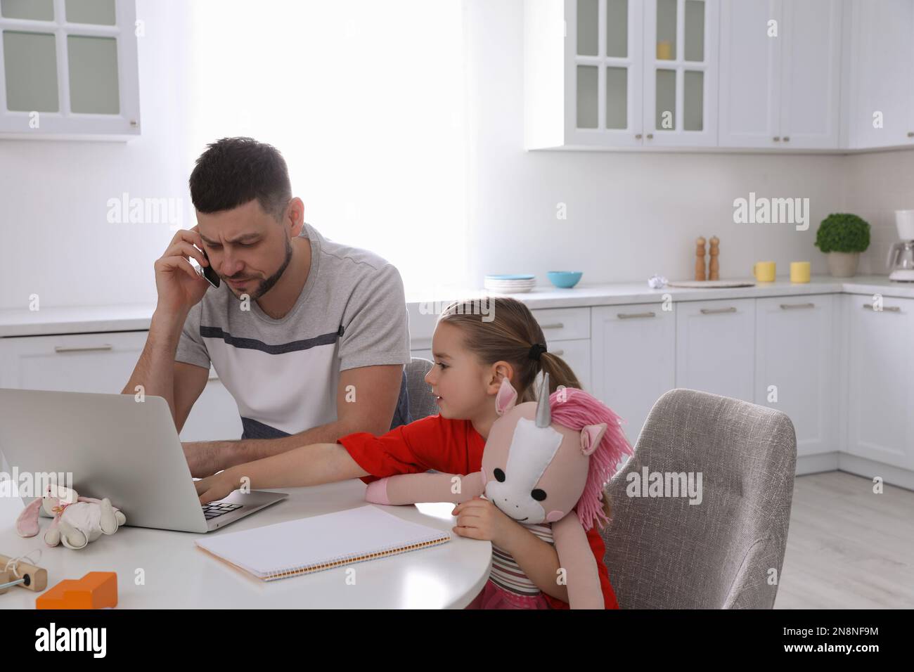 Cute child disturbing stressed man in kitchen. Working from home during ...