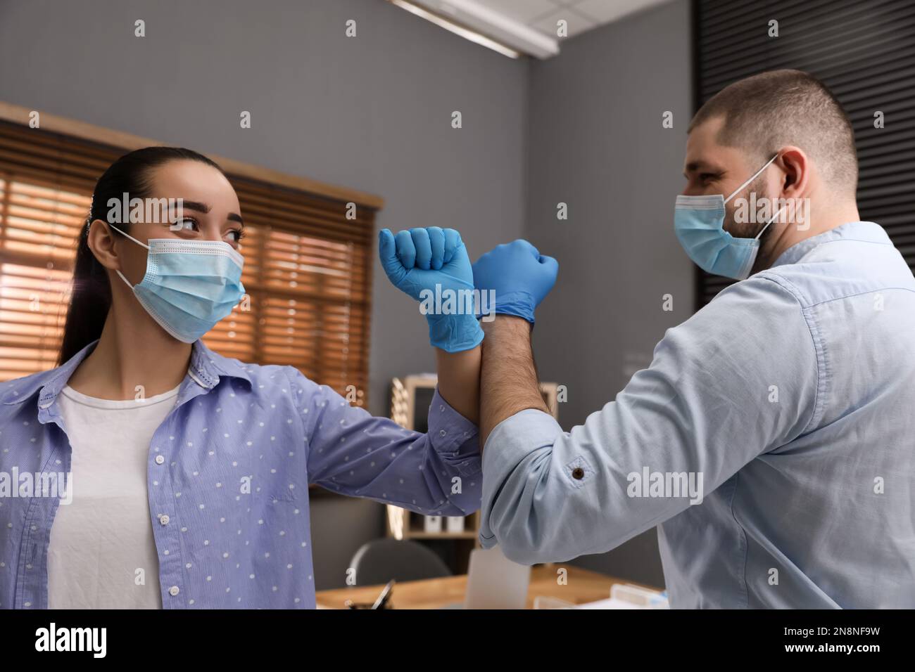Office employees in masks greeting each other by bumping elbows at ...