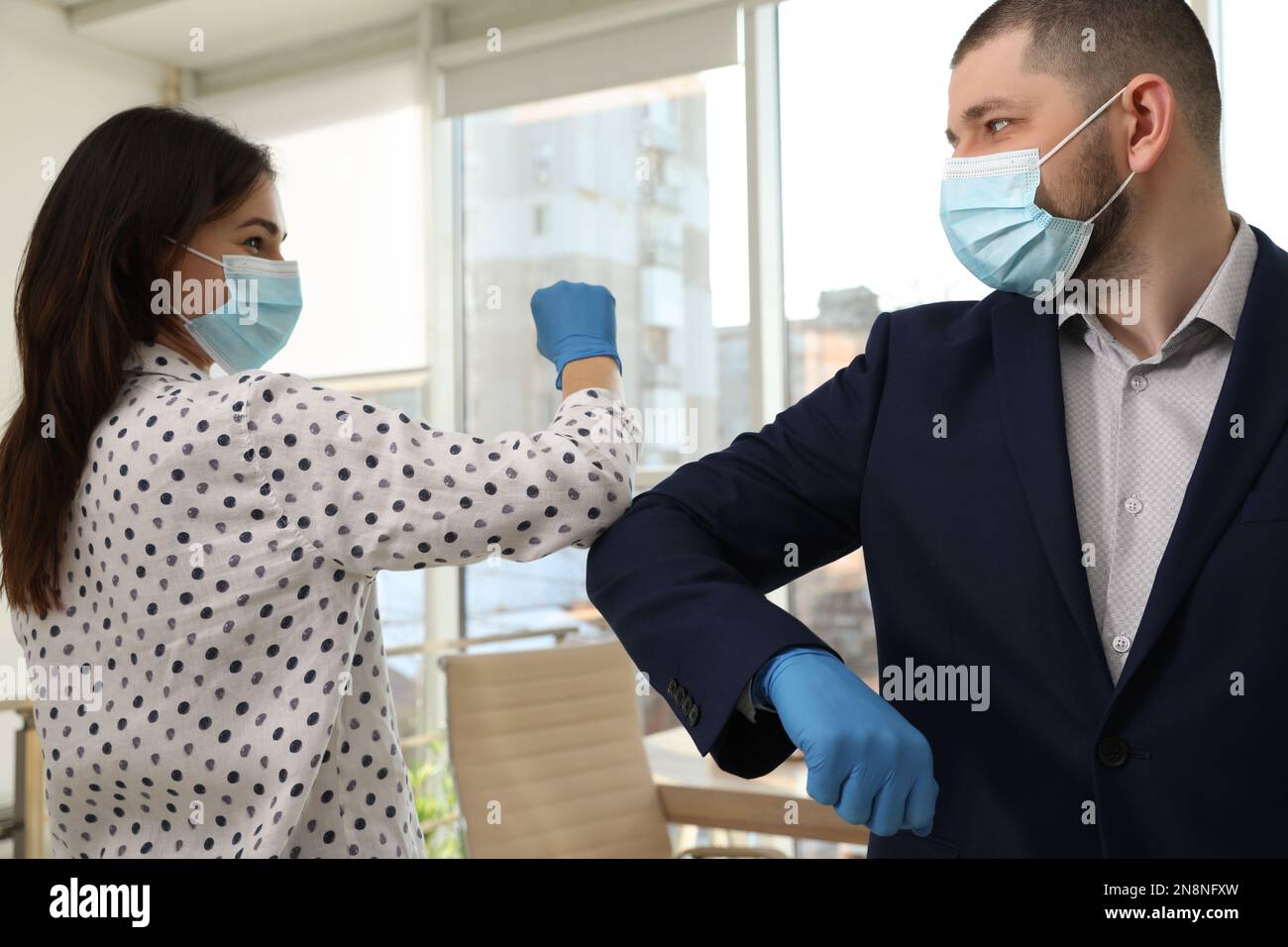 Office employees in masks greeting each other by bumping elbows at ...