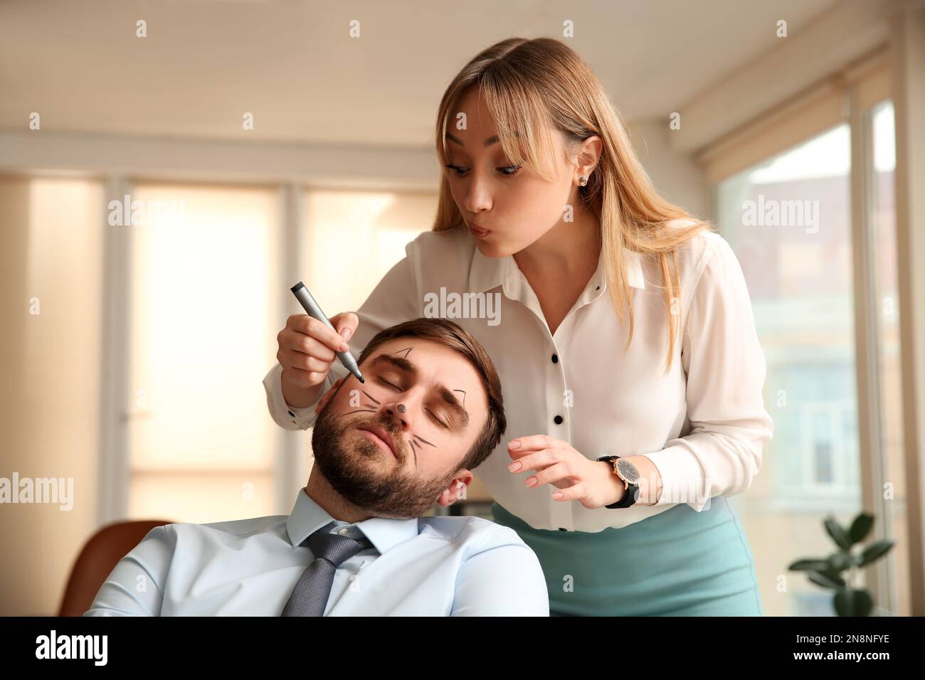 Young woman drawing on colleague's face while he sleeping in office ...