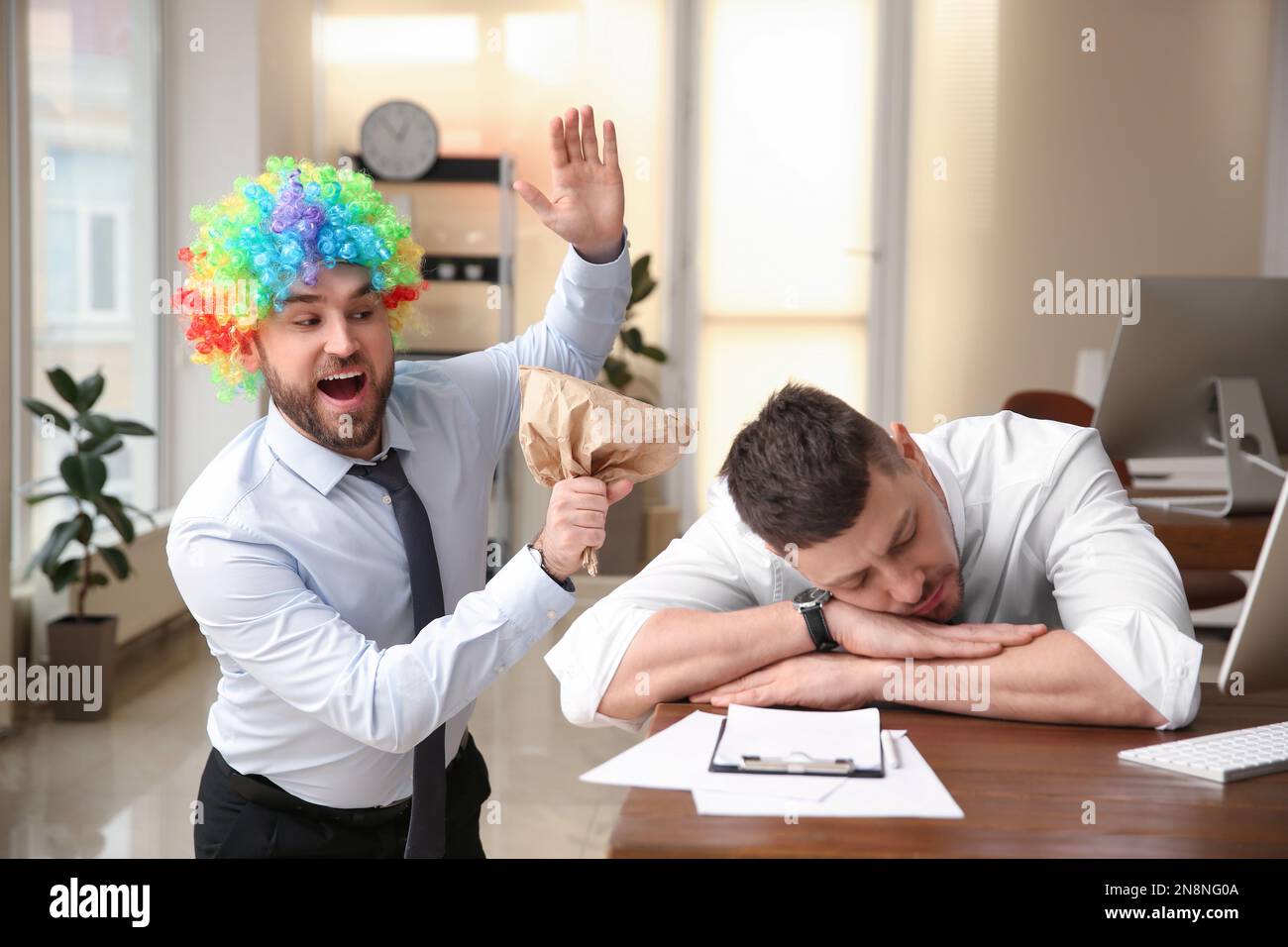 Young man popping paper bag behind his sleeping colleague in office ...