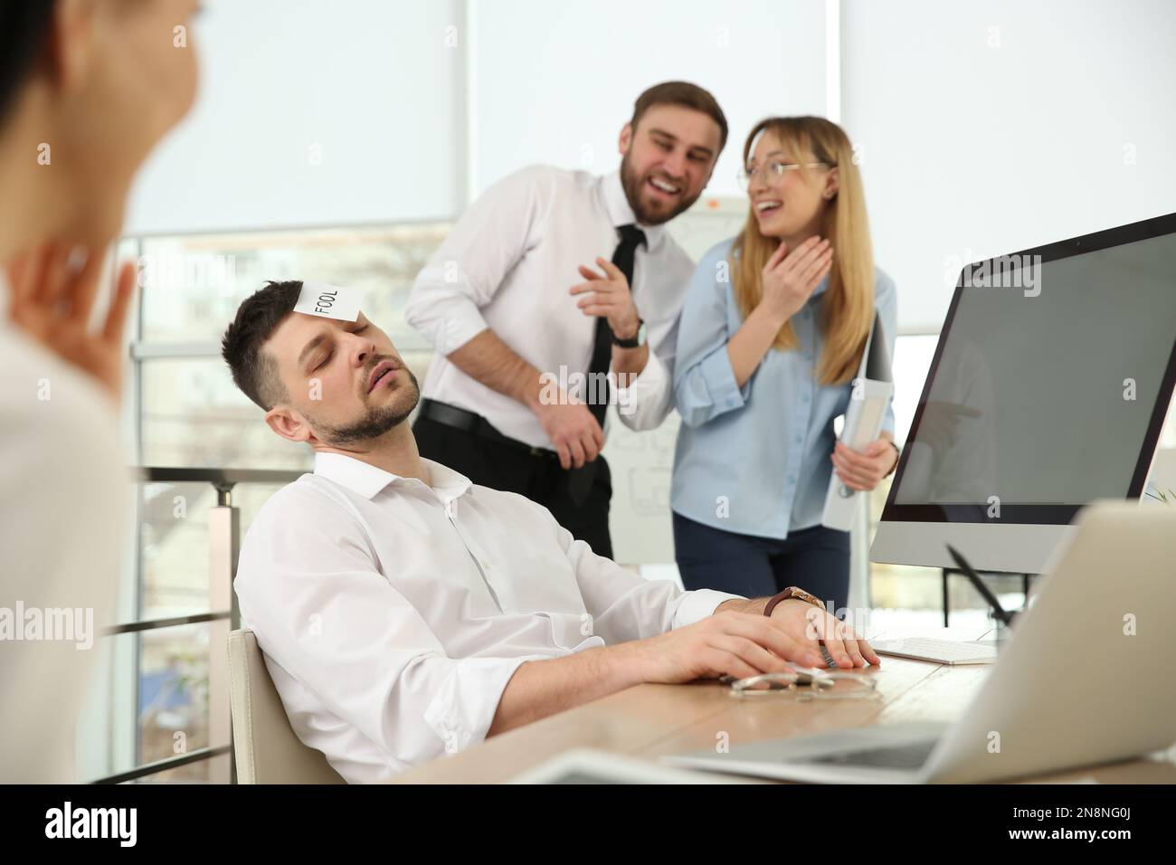 Coworkers sticking note with word Fool to colleague's face in office ...