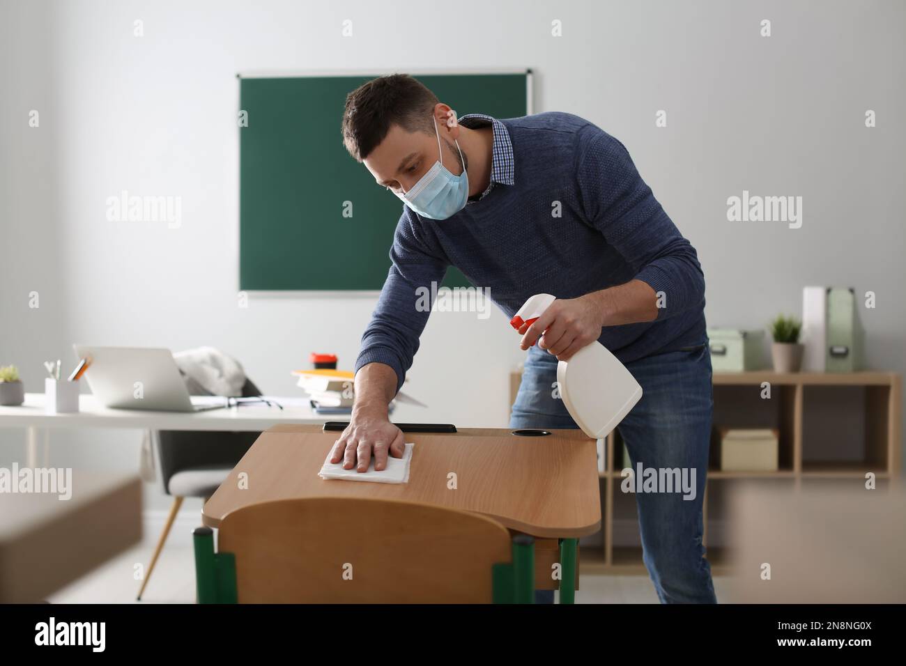 Teacher with protective mask disinfecting desk in classroom. Reopening ...