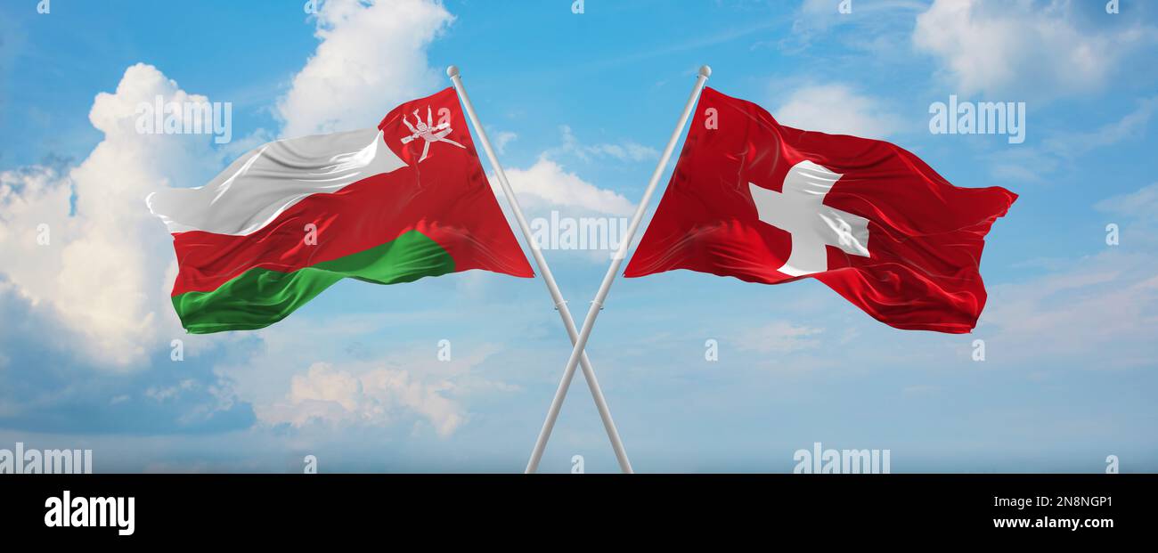 two crossed flags switzerland and Oman waving in wind at cloudy sky ...