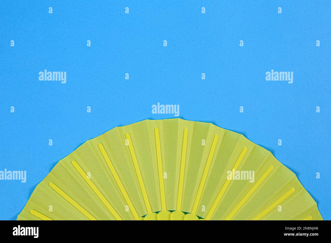 Yellow hand fan on light blue background, top view. Space for text ...