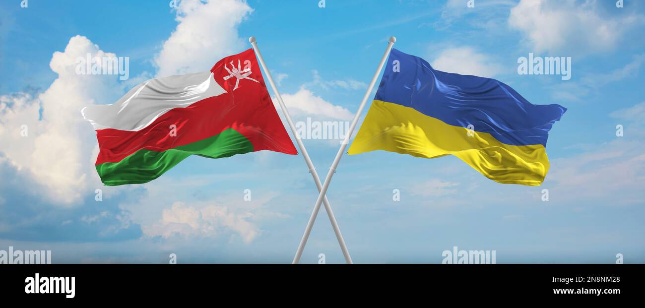 two crossed flags Ukraine and Oman waving in wind at cloudy sky ...