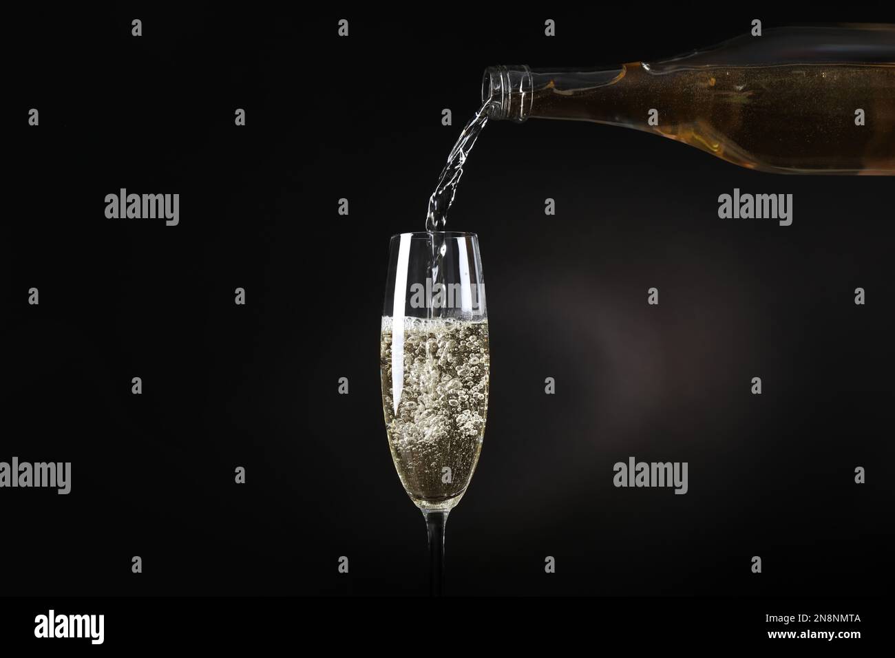 Pouring sparkling wine from bottle into glass on black background Stock Photo - Alamy