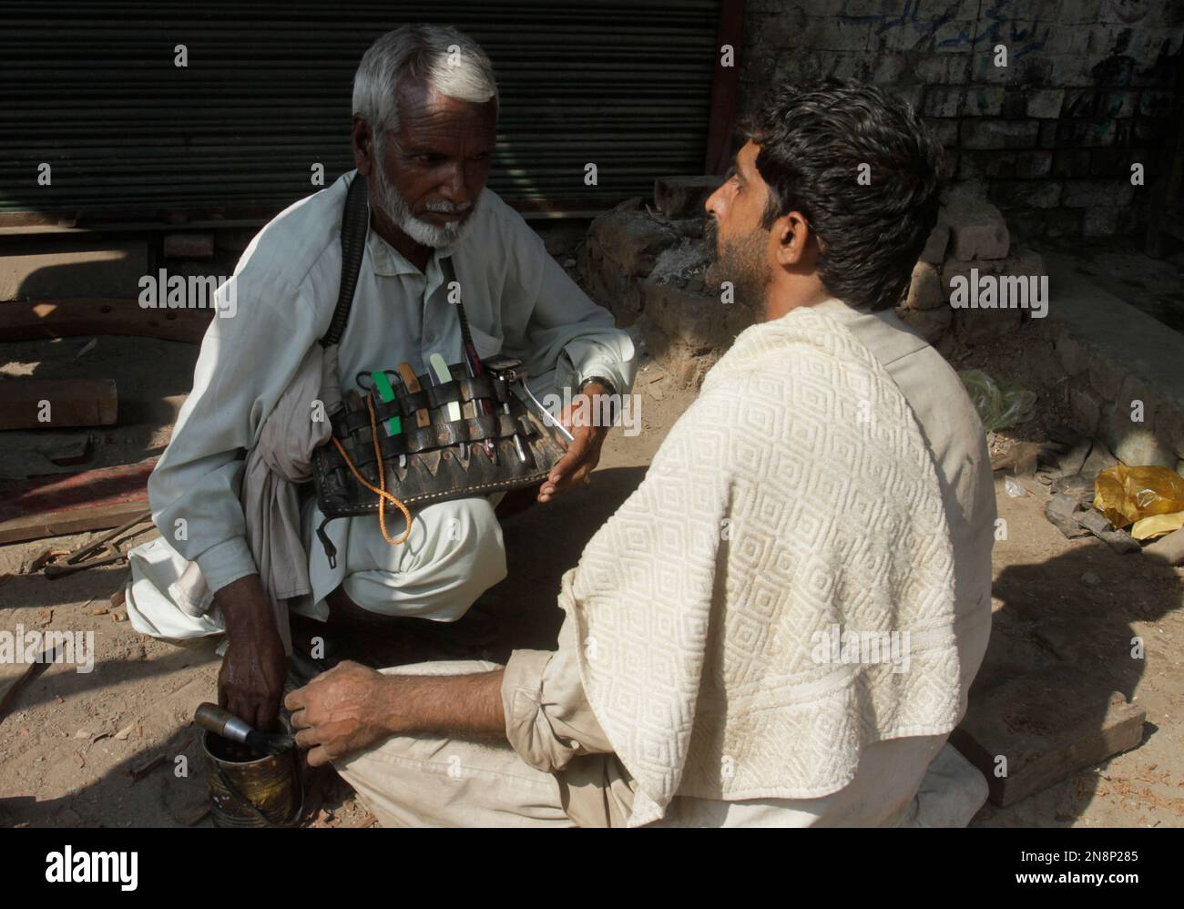 A Pakistani street barber prepare to cut a customer's hair, along a ...