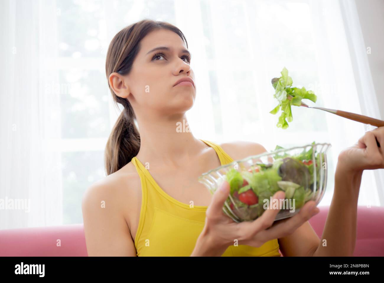 Young caucasian woman sitting on sofa eating vegetable salad while ...