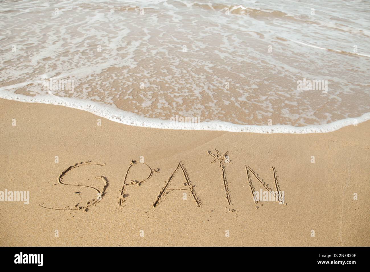 Spain lettering on the beach with wave and clear blue sea Stock Photo ...
