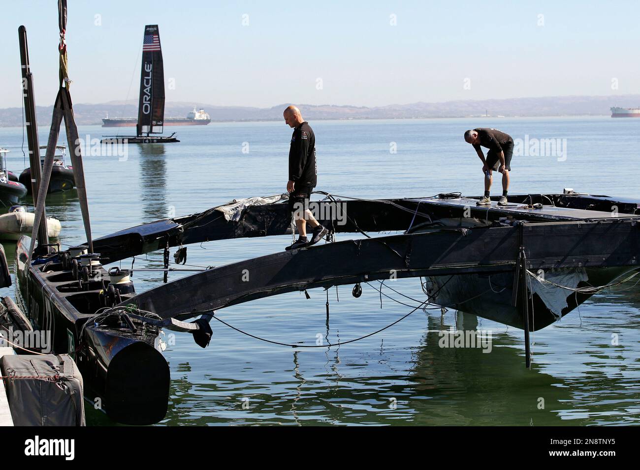Crew members look over the hull remains of a capsized Oracle Team USA ...
