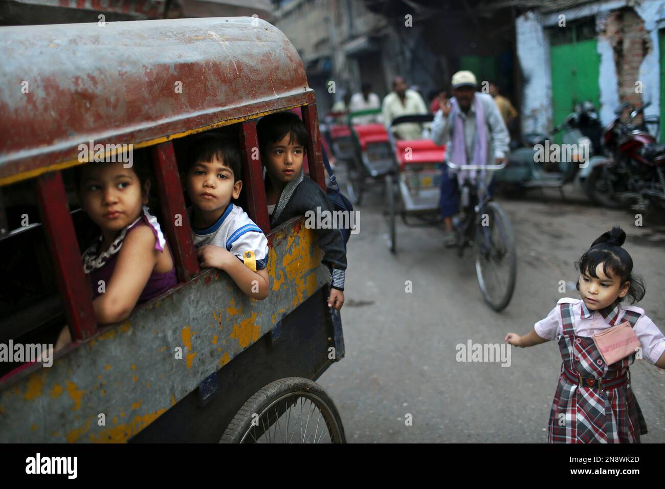 Indian school children wait in the back of a bicycle rickshaw as they ...