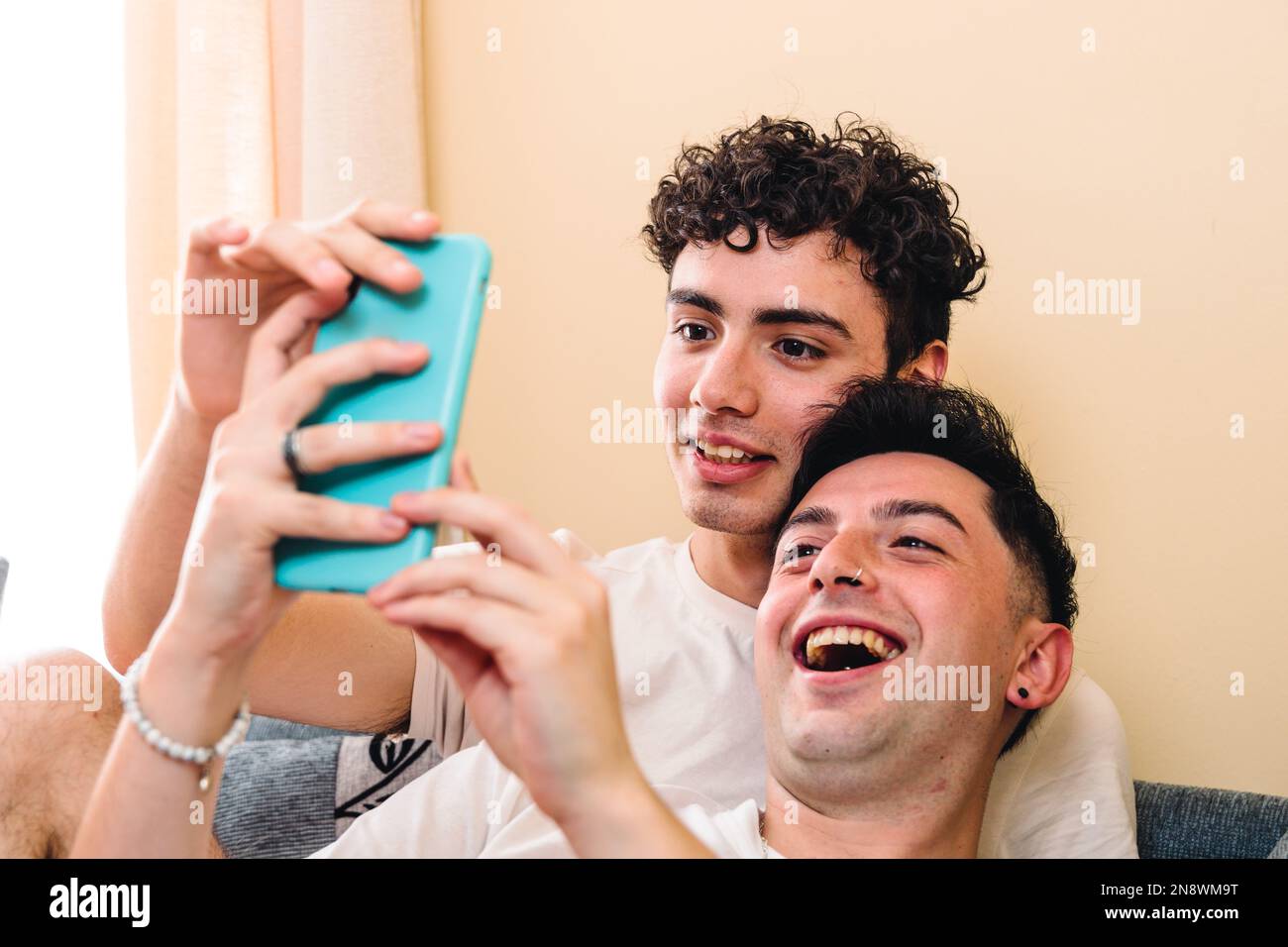 Young smiling gay couple using the smart phone to watch entertaining ...