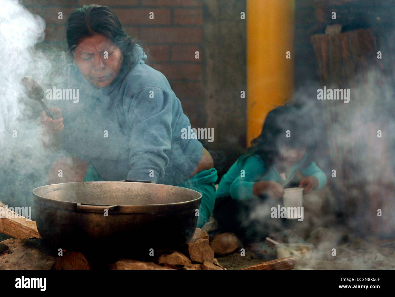 A woman tends a campfire as she prepares fried fish, part of the ...