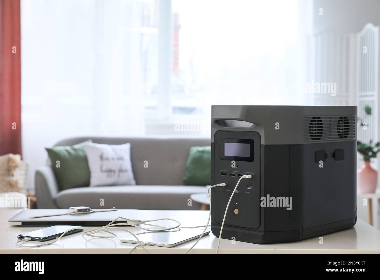 Portable power station charging gadgets on table in living room Stock ...