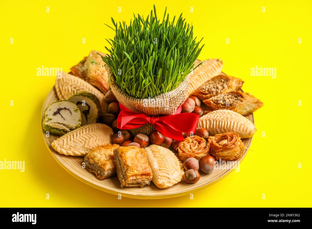 Plate with treats and grass on yellow background. Novruz Bayram ...