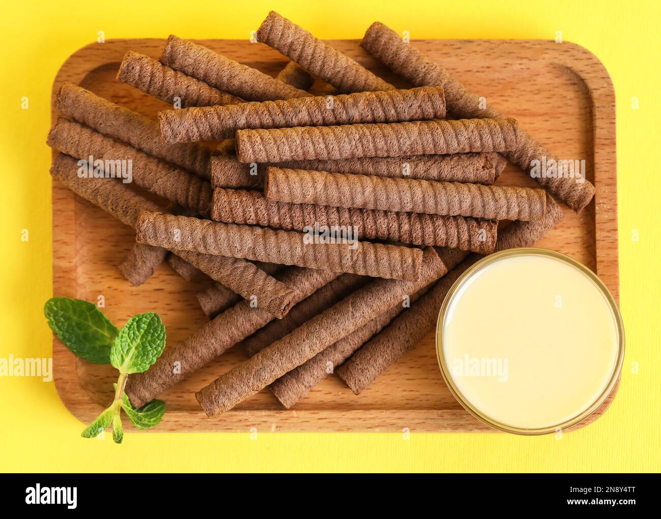 Board with delicious chocolate wafer rolls and condensed milk on yellow ...