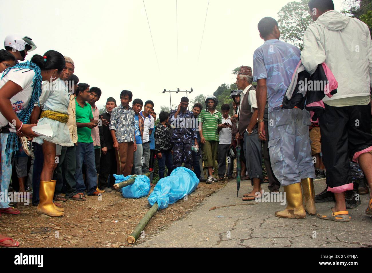 Nepalese villagers stand near wrapped bodies of landslide victims near ...