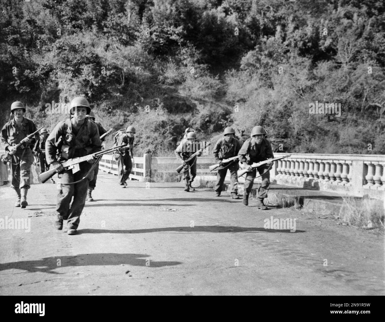 Crouching as they move out into the open, Yank troops cross the bridge ...
