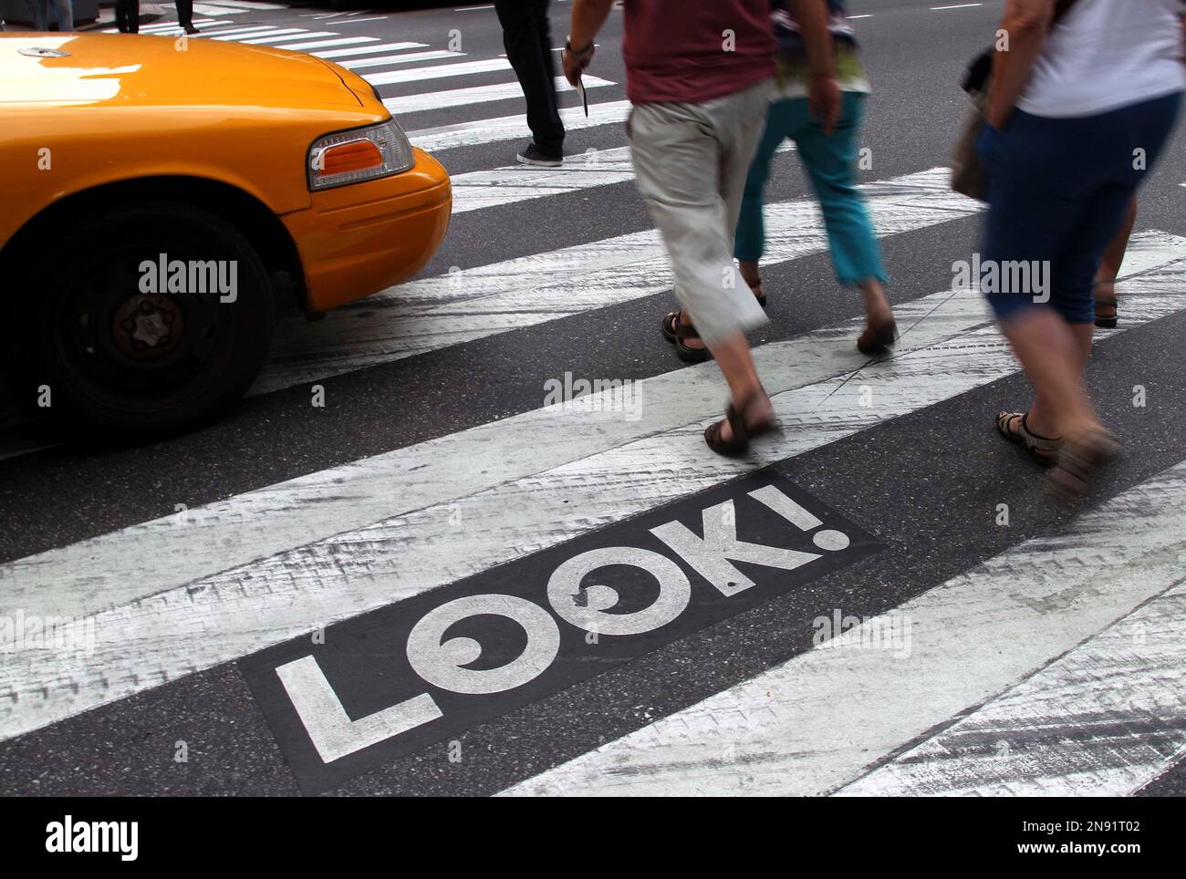 Pedestrians walk past a "Look!" sign on the crosswalk at the ...