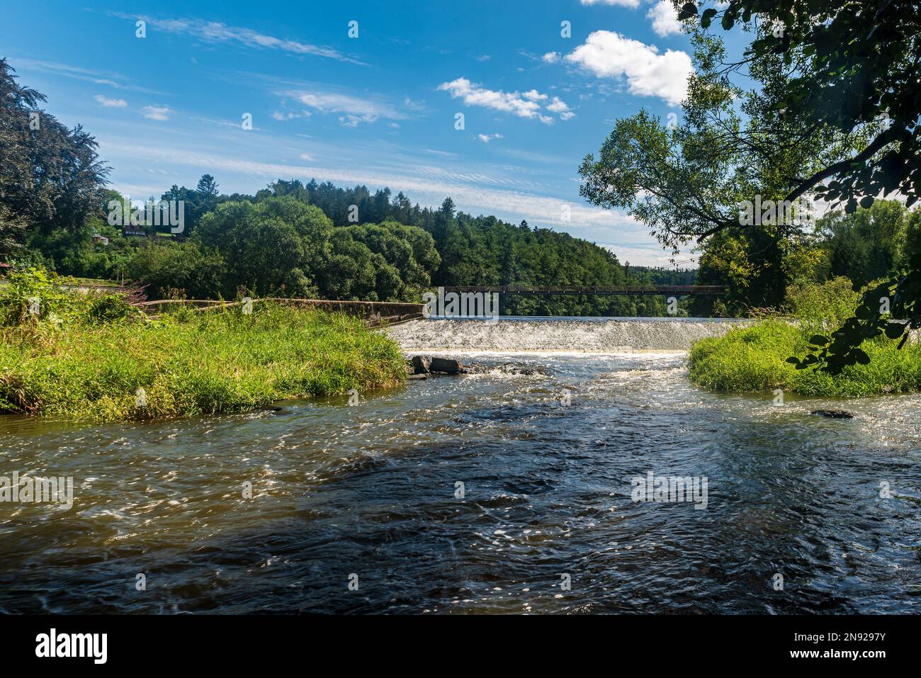 River with weir, bridge above and trees around during beautiful summer ...