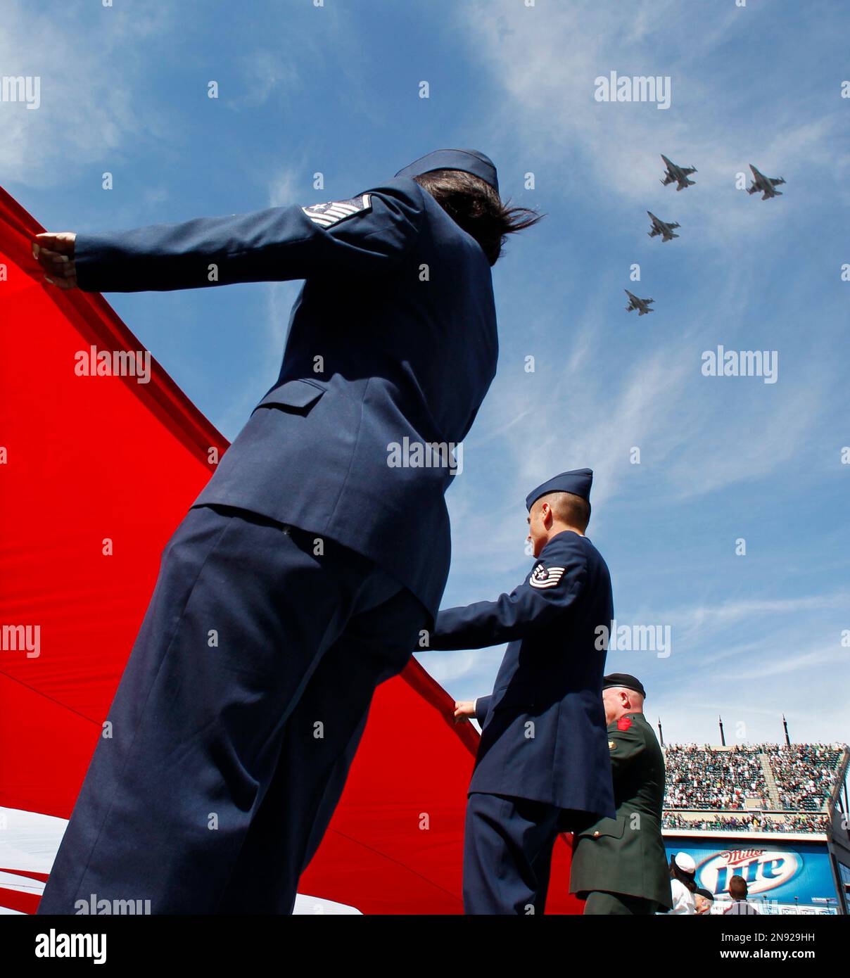 A fighter jets do a fly-over, military personnel hold a giant American ...