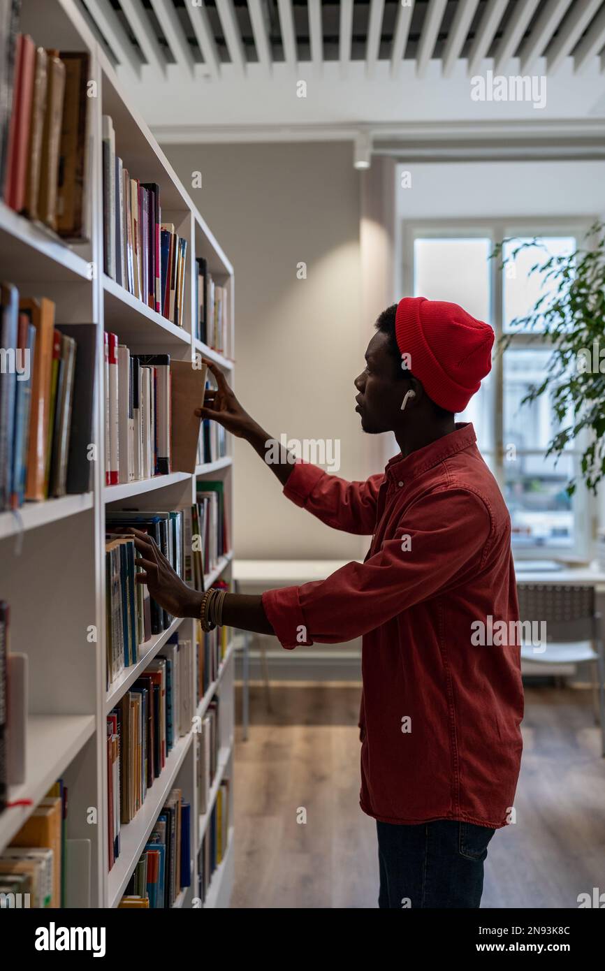African American student man picking up book from shelf while standing ...